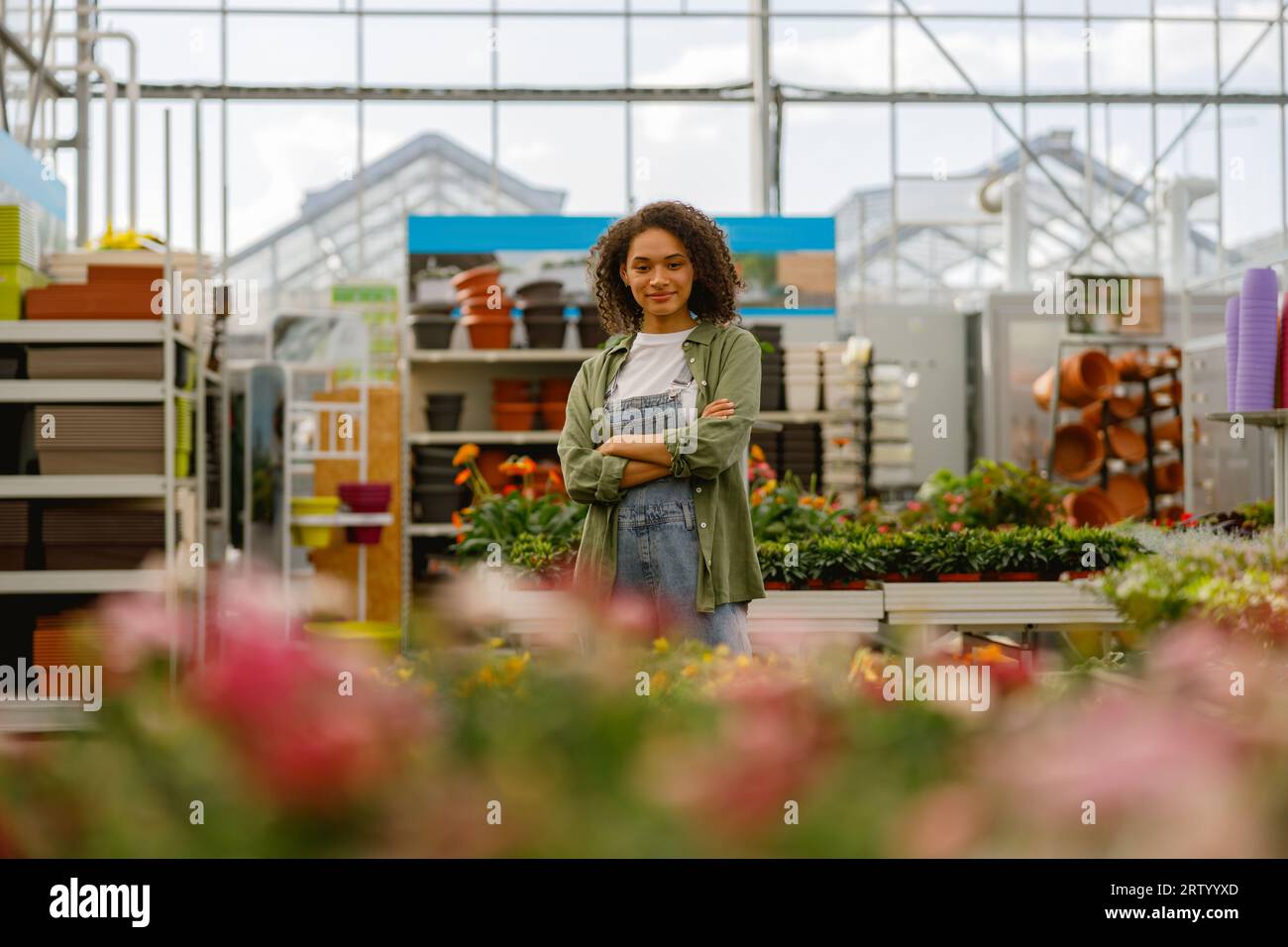 Smiling female garden shop seller standing with crossed hands on flower ...
