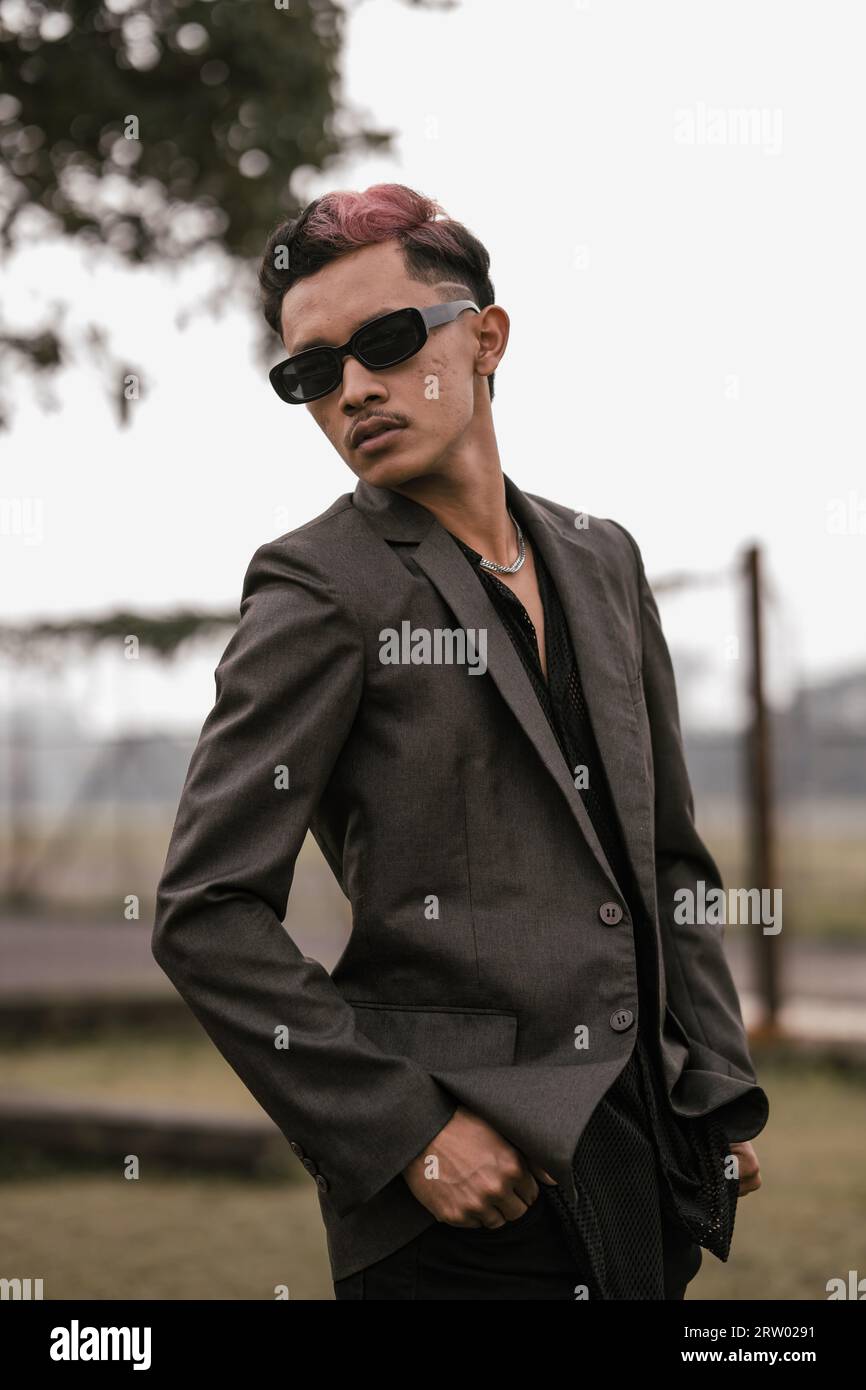 an Asian man with sunglasses posing in a gray suit in the yard at noon ...