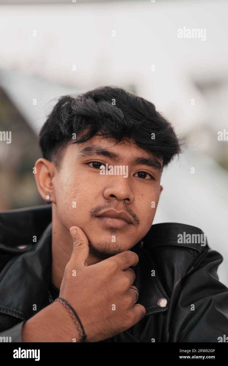 an Asian man with a naughty face wearing a chain necklace and a black leather jacket in a cafe ...