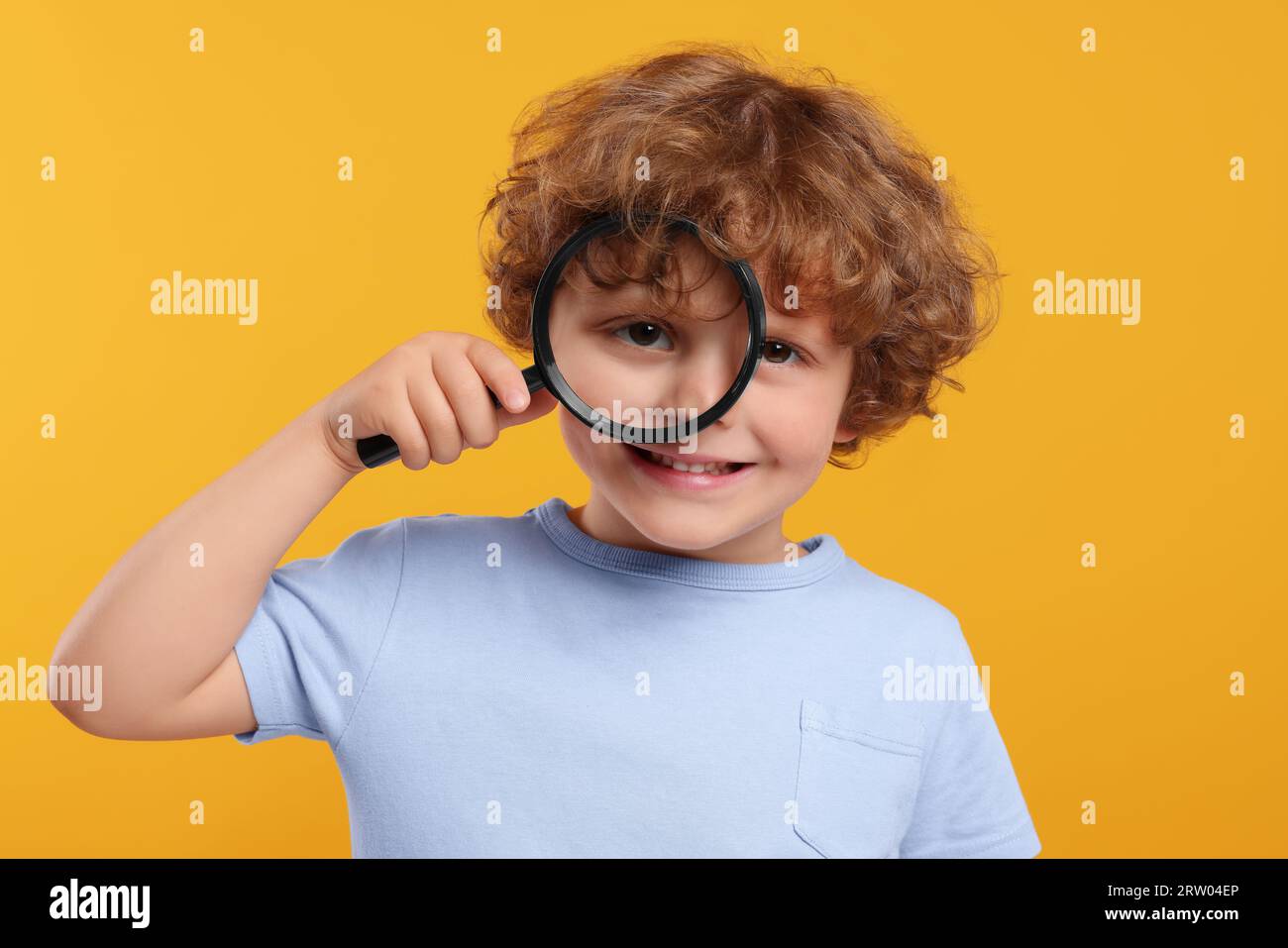 Cute little boy looking through magnifier glass on orange background ...