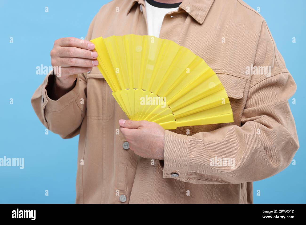 Man holding hand fan on light blue background, closeup Stock Photo - Alamy
