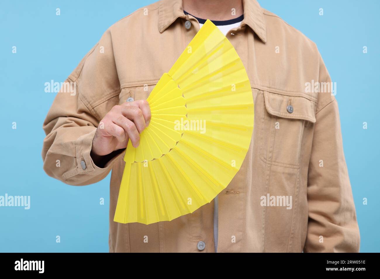Man holding hand fan on light blue background, closeup Stock Photo - Alamy