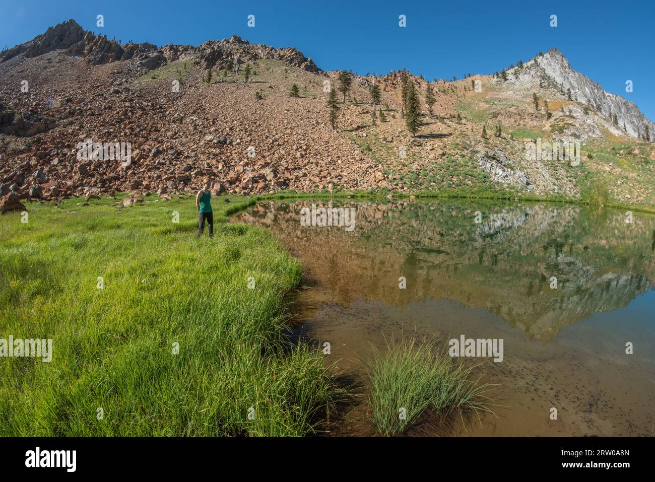 A hiker stands at the edge of a high elevation lake in the trinity alps ...