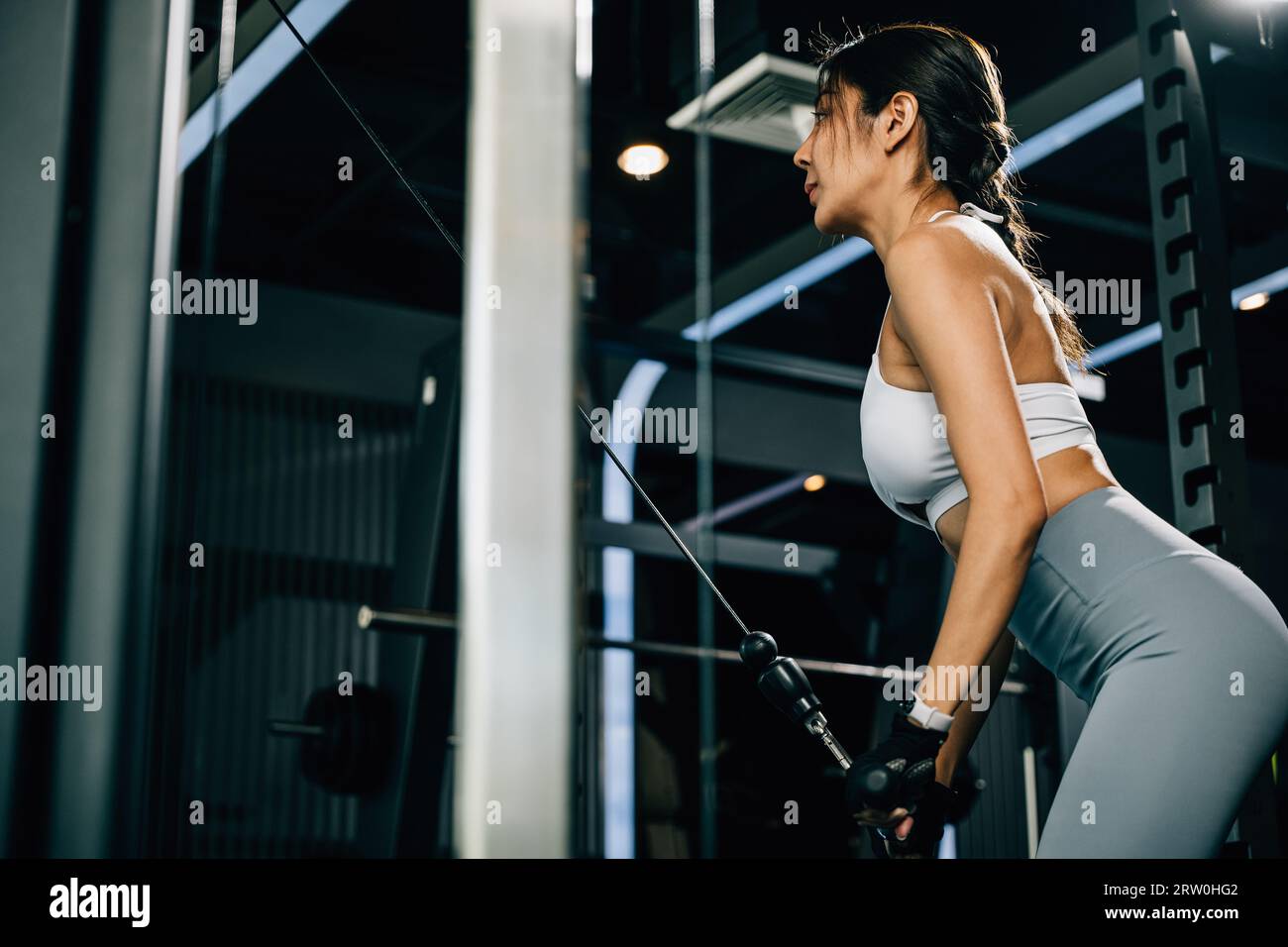 Slim and strong young woman working out on a pull-down weight machine ...