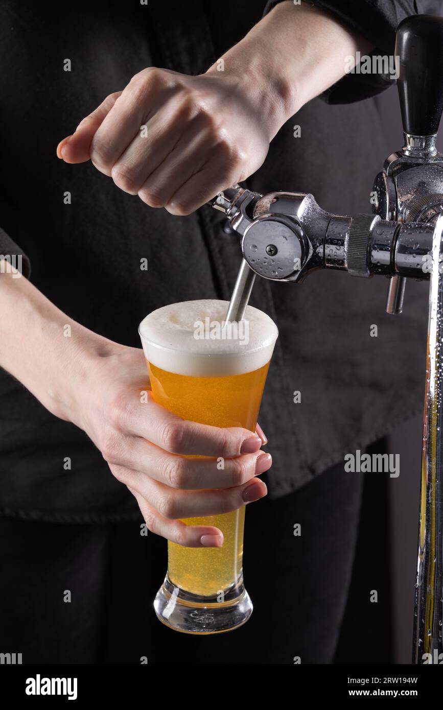 The bartender pours fresh beer from the tap into a glass on a dark ...