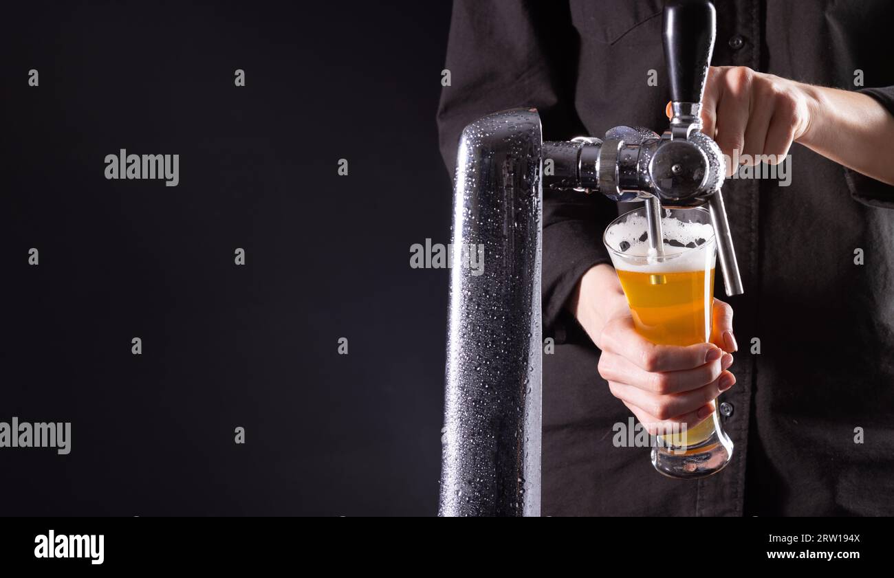 The bartender pours fresh beer from the tap into a glass on a dark ...