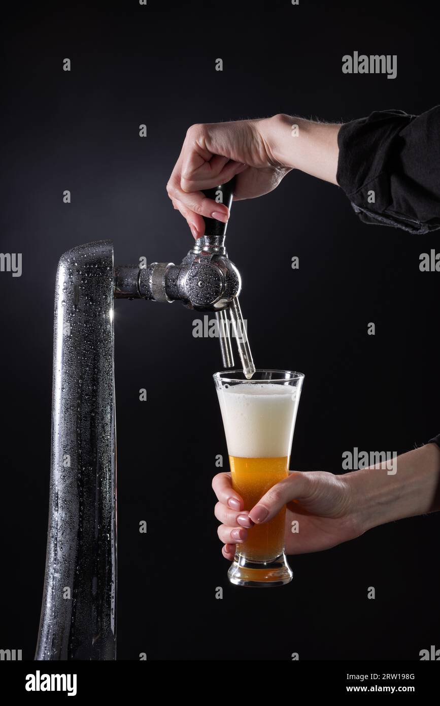 The bartender pours fresh beer from the tap into a glass on a dark ...