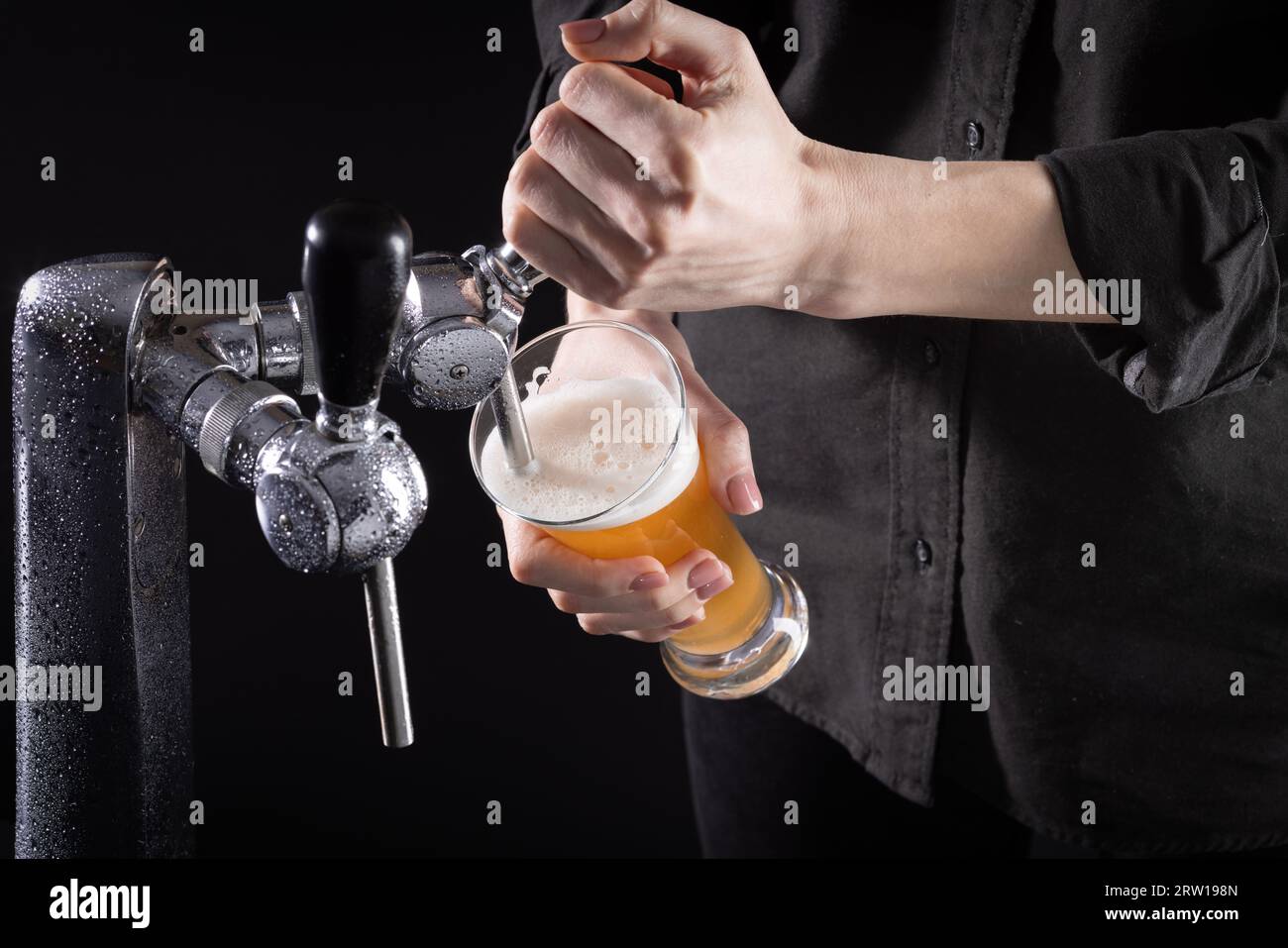The bartender pours fresh beer from the tap into a glass on a dark ...