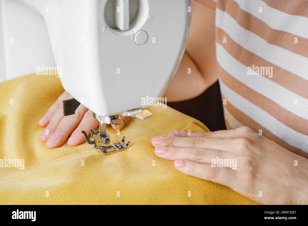 Tailor hands stitching yellow fabric on modern sewing machine at workplace in atelier. Women's ...