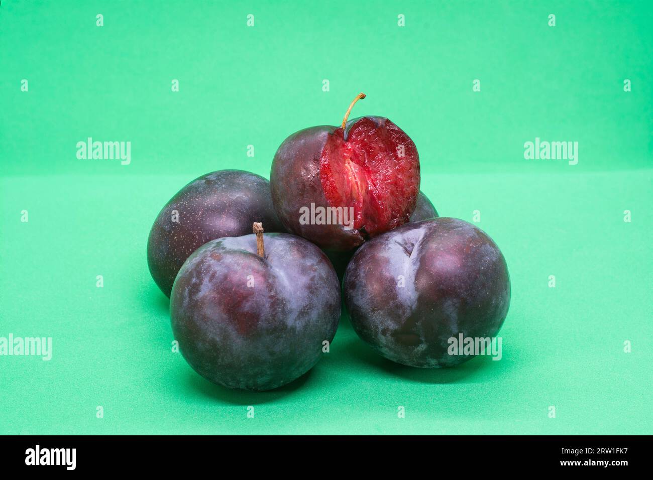 Ripe plums against a green background, with a bite taken from one Stock ...