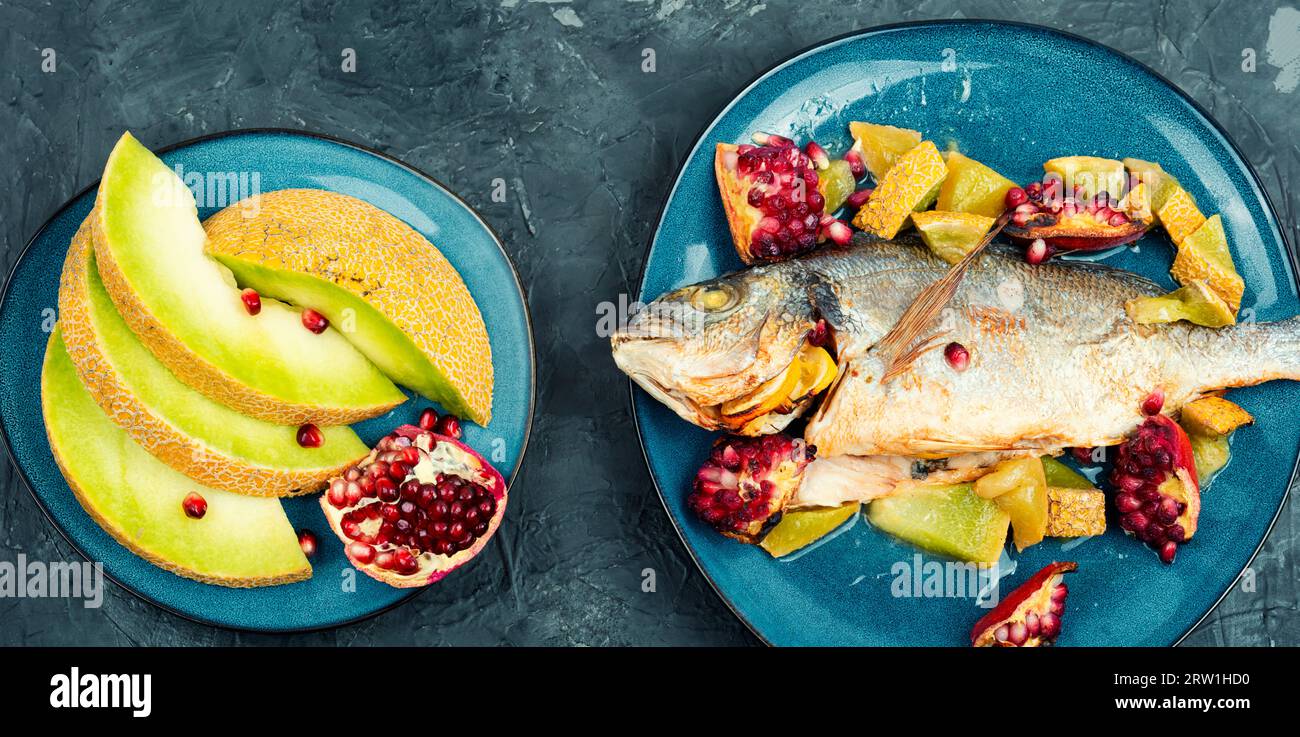 Baked dorado fish with melon and pomegranate on concrete table. Food ...