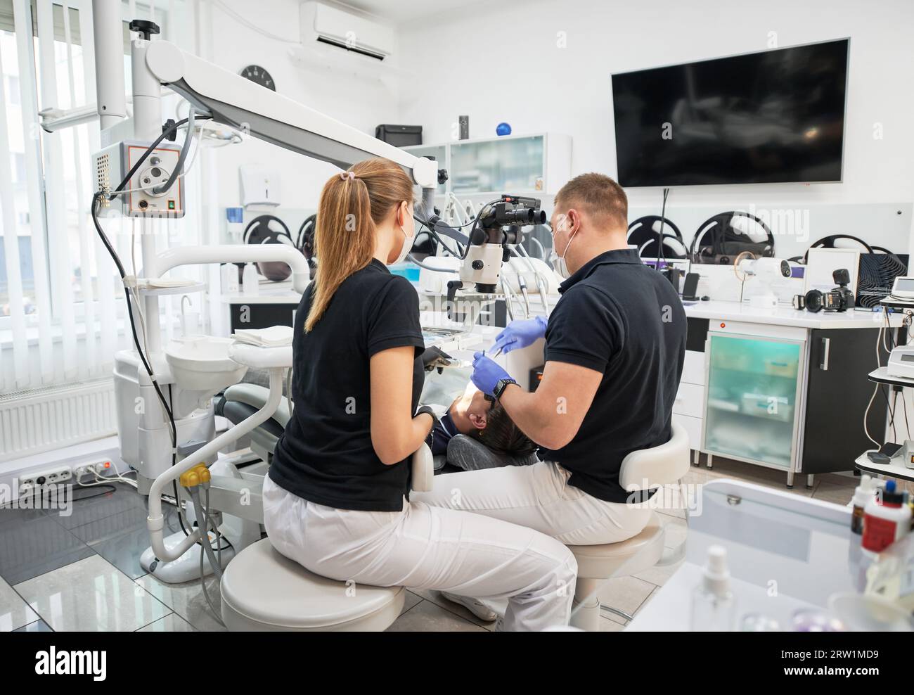 Back view of concentrated dentists sitting on chairs, fixing teeth. Two ...
