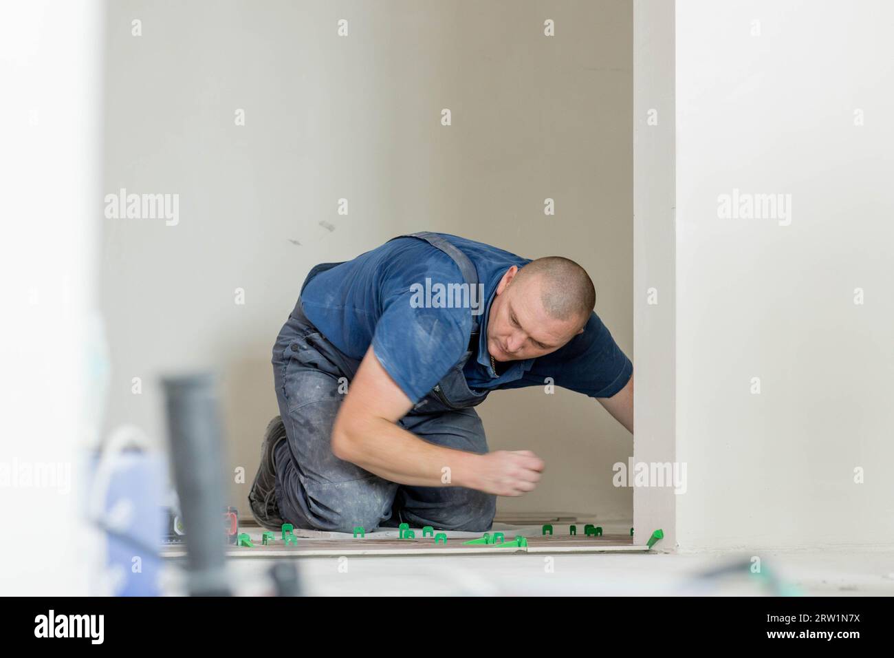 Tiler placing ceramic wall tile in position over adhesive with lash ...