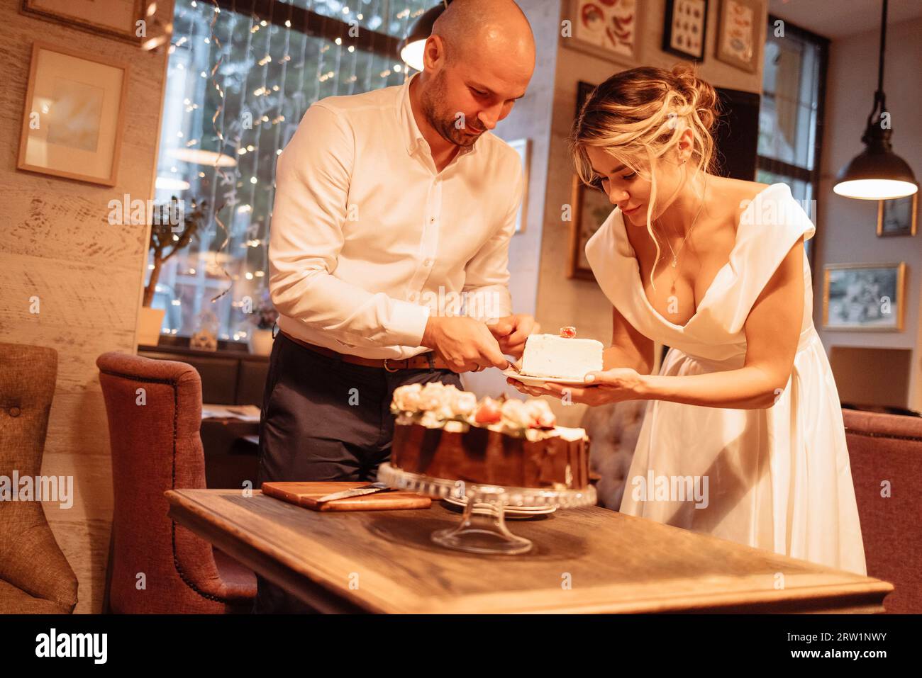 Attractive groom and charming bride are cutting festive wedding cake ...
