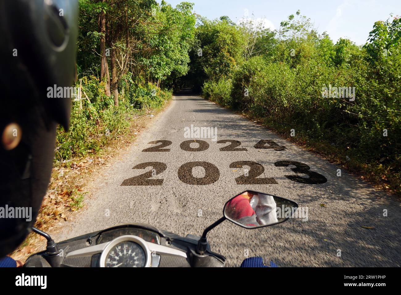 Black asphalt road with new year numbers 2023, 2024 with motorbike riders passing on a quiet and ...