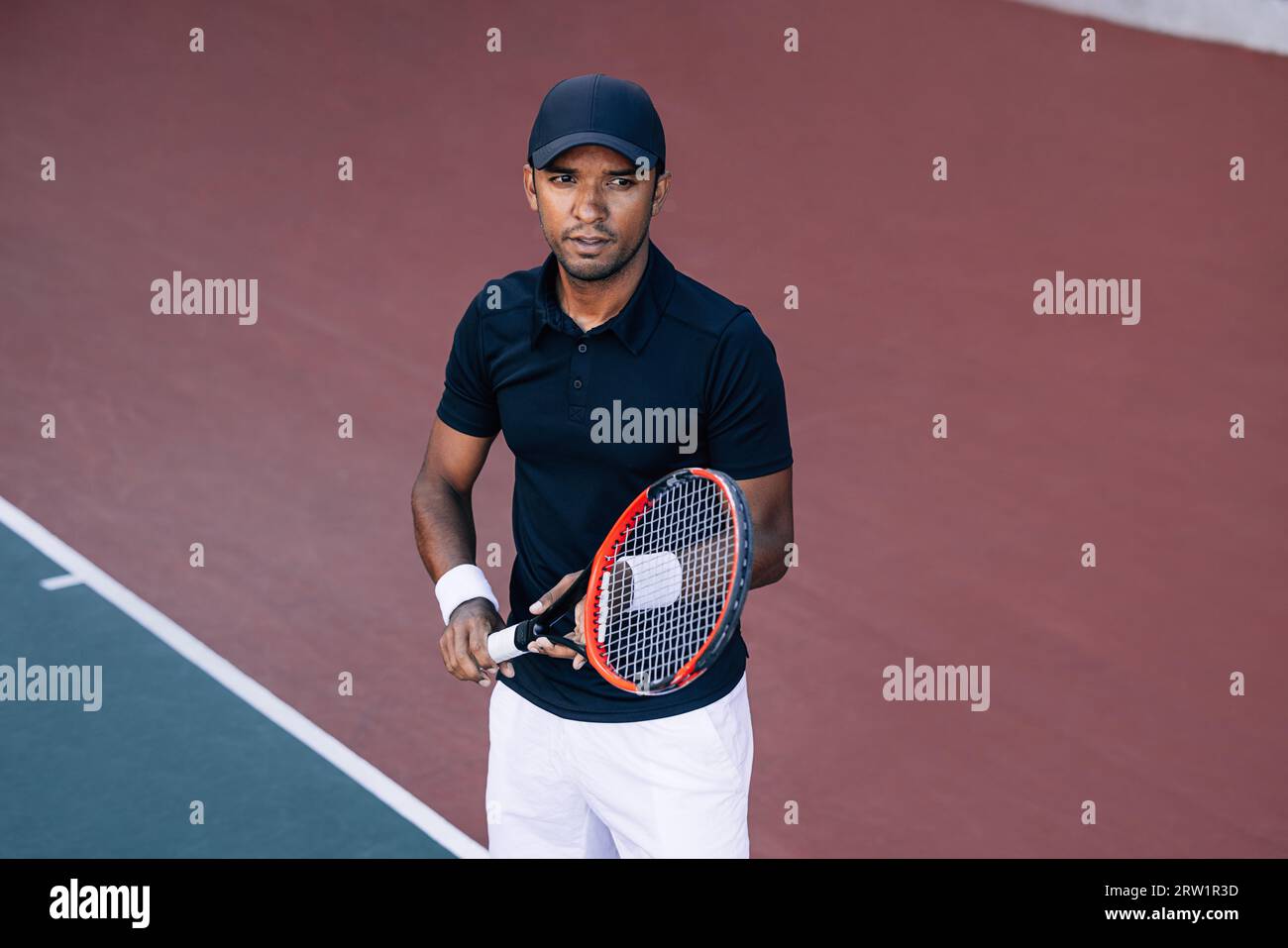 Portrait of a young tennis player with a racket standing on a hard ...