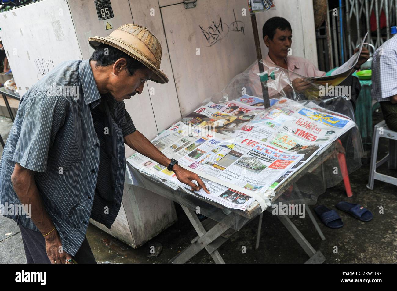 26.07.2013, Myanmar, Yangon, Yangon - A newspaper vendor sits behind ...