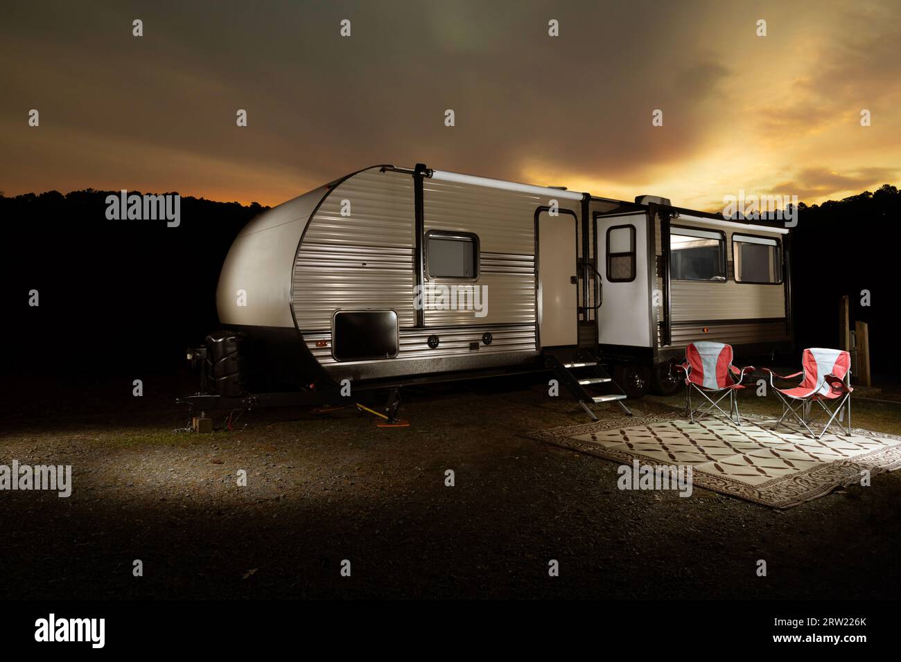 RV at a campsite at with a solorful sunset behind and trees silhouetted ...
