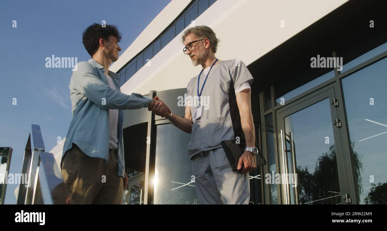 Mature doctor with tablet in hands stands with patient at clinic ...