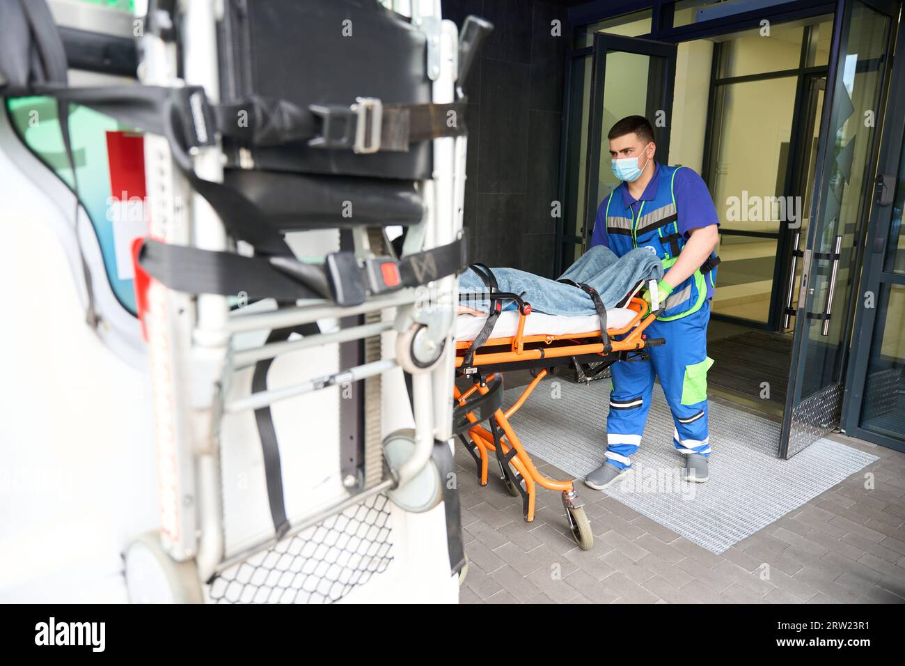 Paramedic in protective mask unloads stretcher with patient from ...