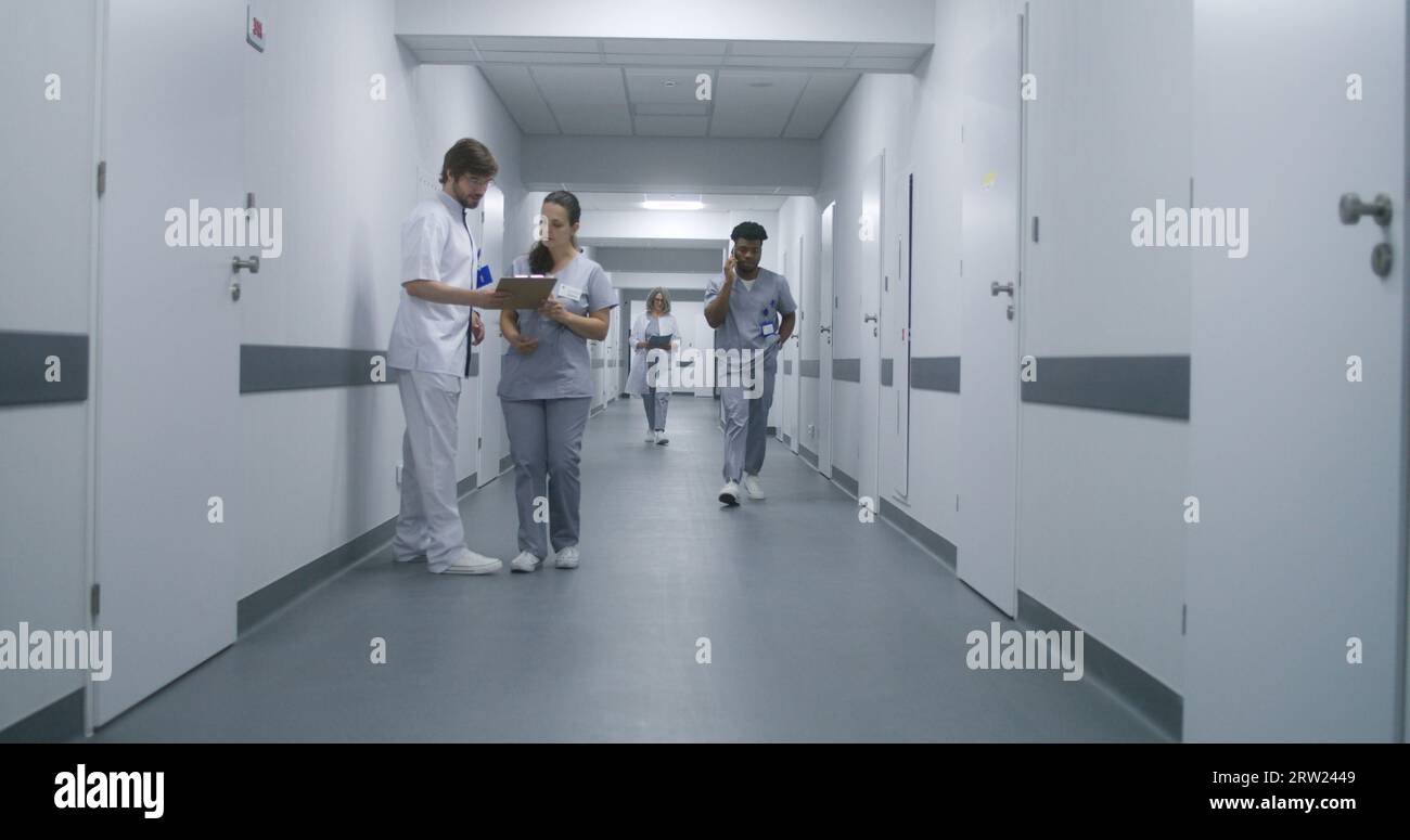 Multiracial medical staff in uniform walk clinic corridor. Elderly ...