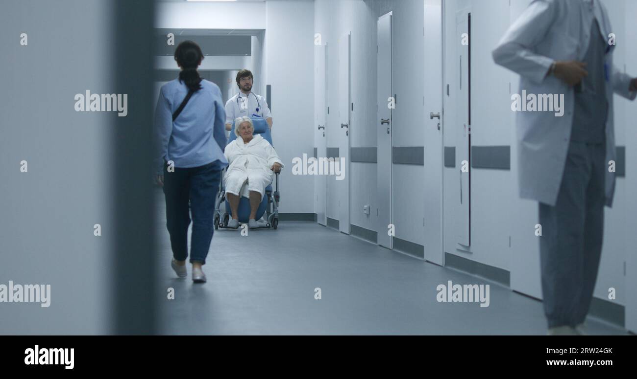 Doctor pushes wheelchair with female patient walking along clinic ...