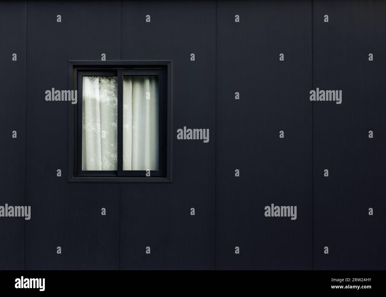 Dark grey facade and illuminated window with cream-colored sheer ...