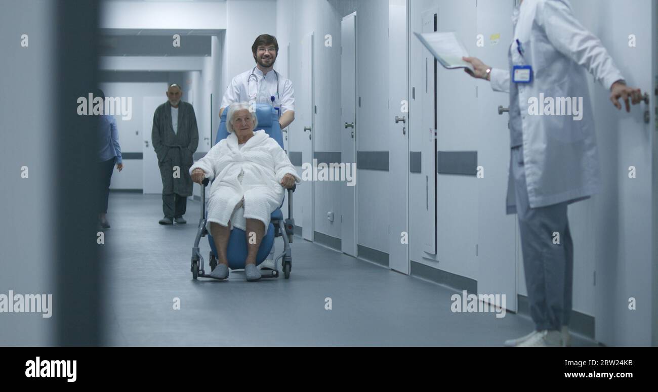 Doctor pushes wheelchair with female patient walking along clinic ...