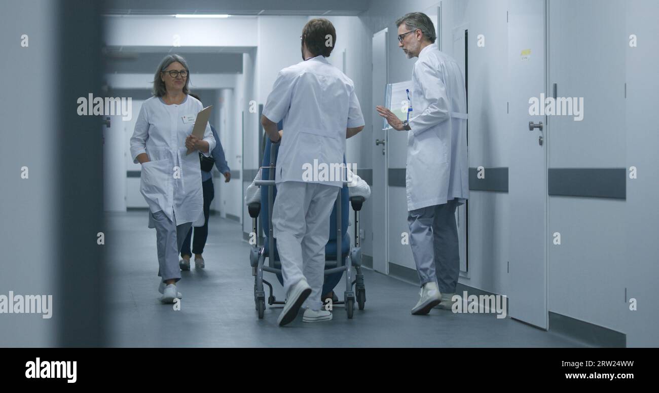 Back view of doctors pushing transfer wheelchair with patient walking ...