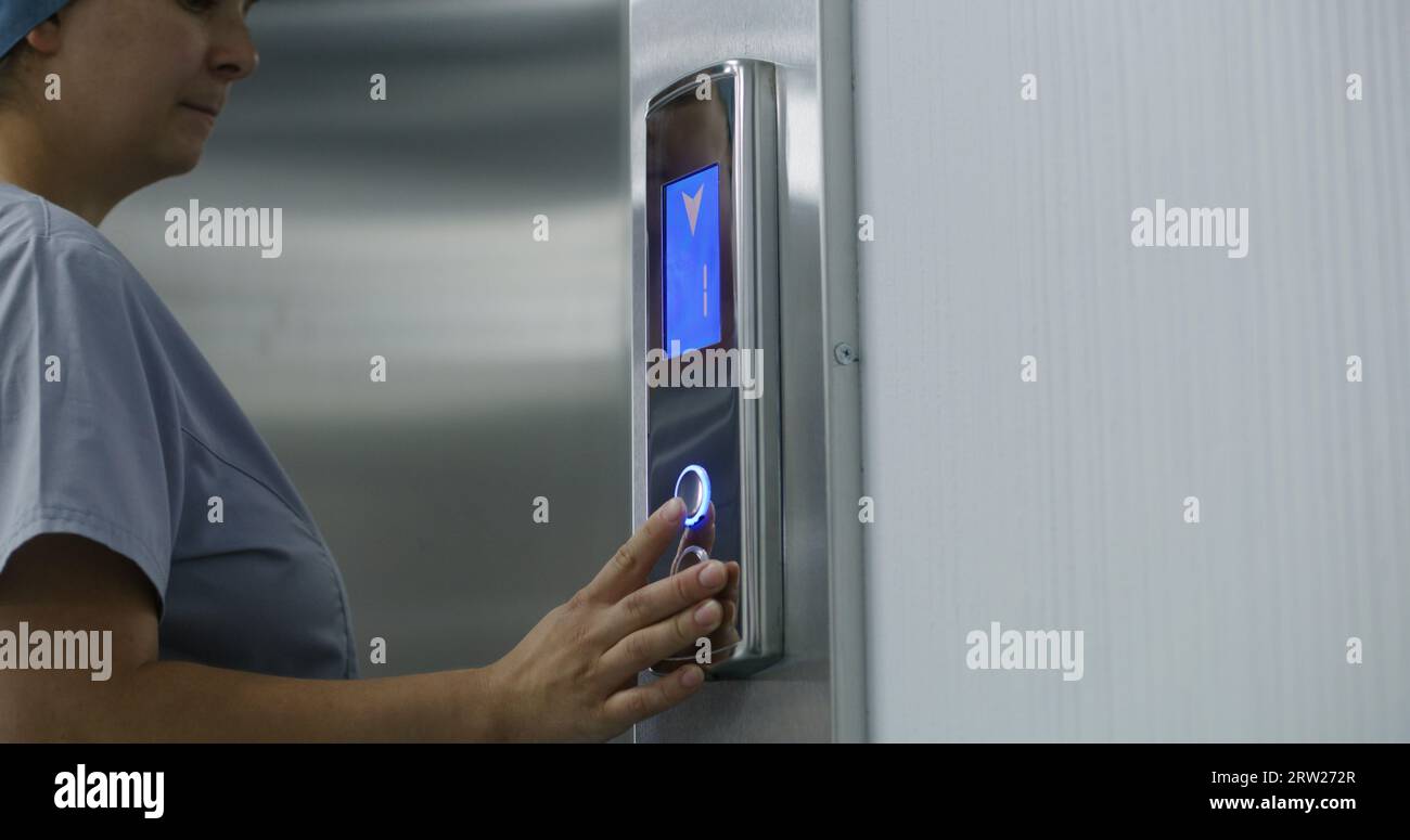 Close up shot of nurse in uniform coming to lift door, pressing call ...