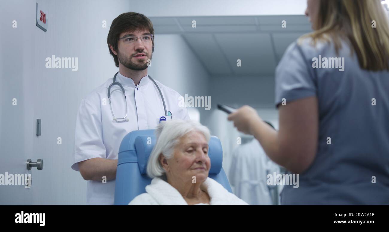 Male doctor stands in clinic corridor with elderly woman in transfer ...