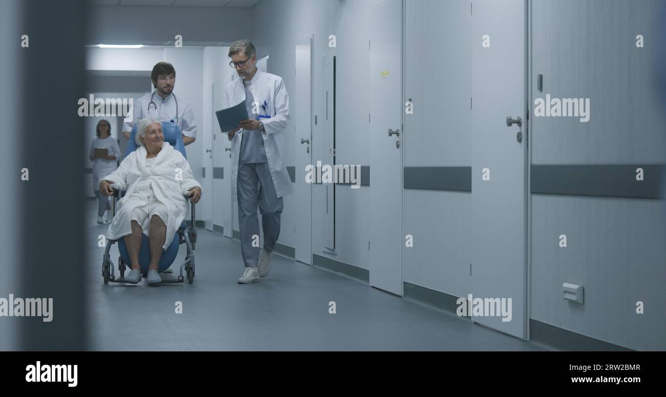 Back view of doctors pushing transfer wheelchair with patient walking ...