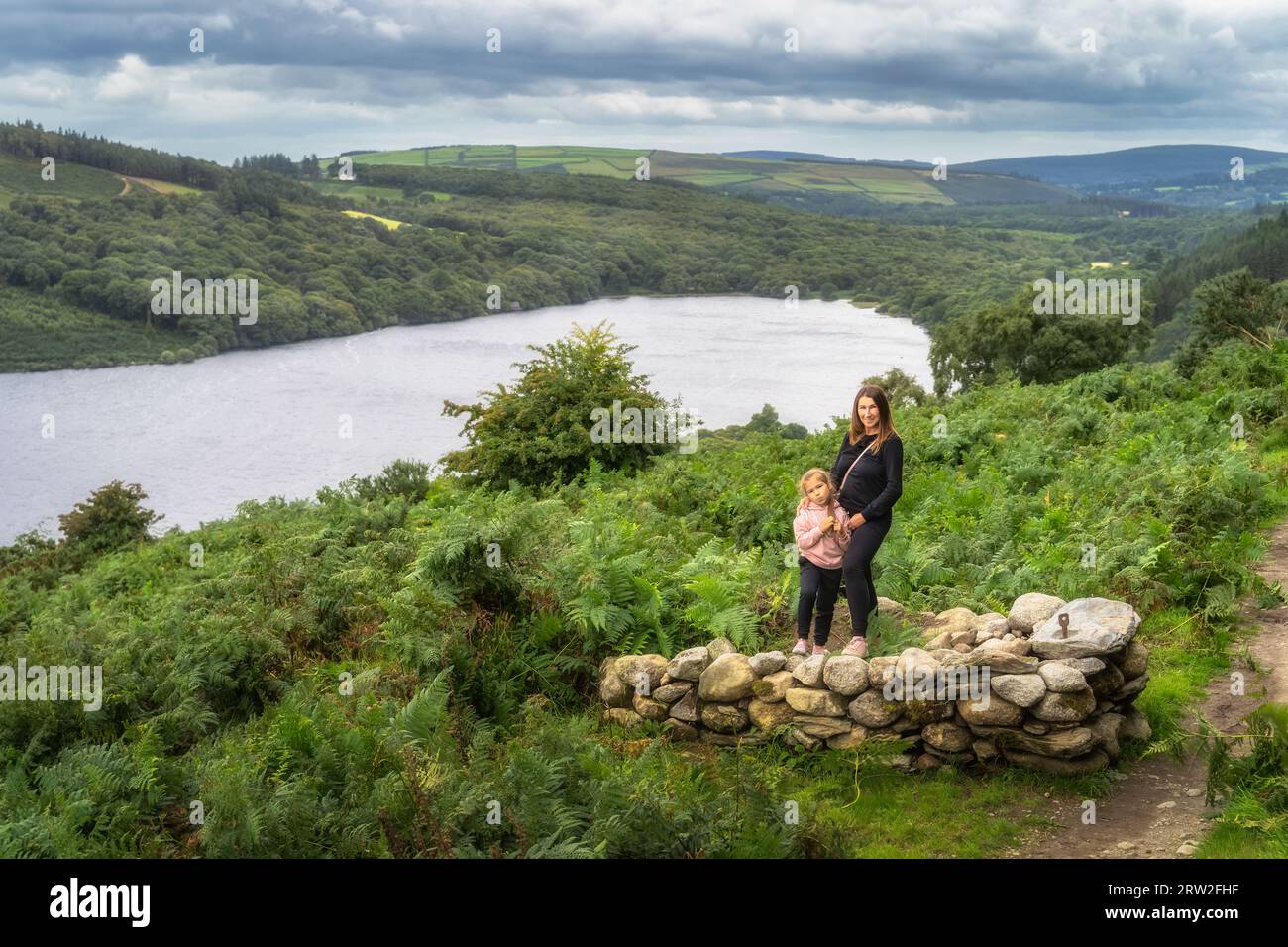Mother and daughter standing on rocks, with lake, Lough Dan, forest and ...