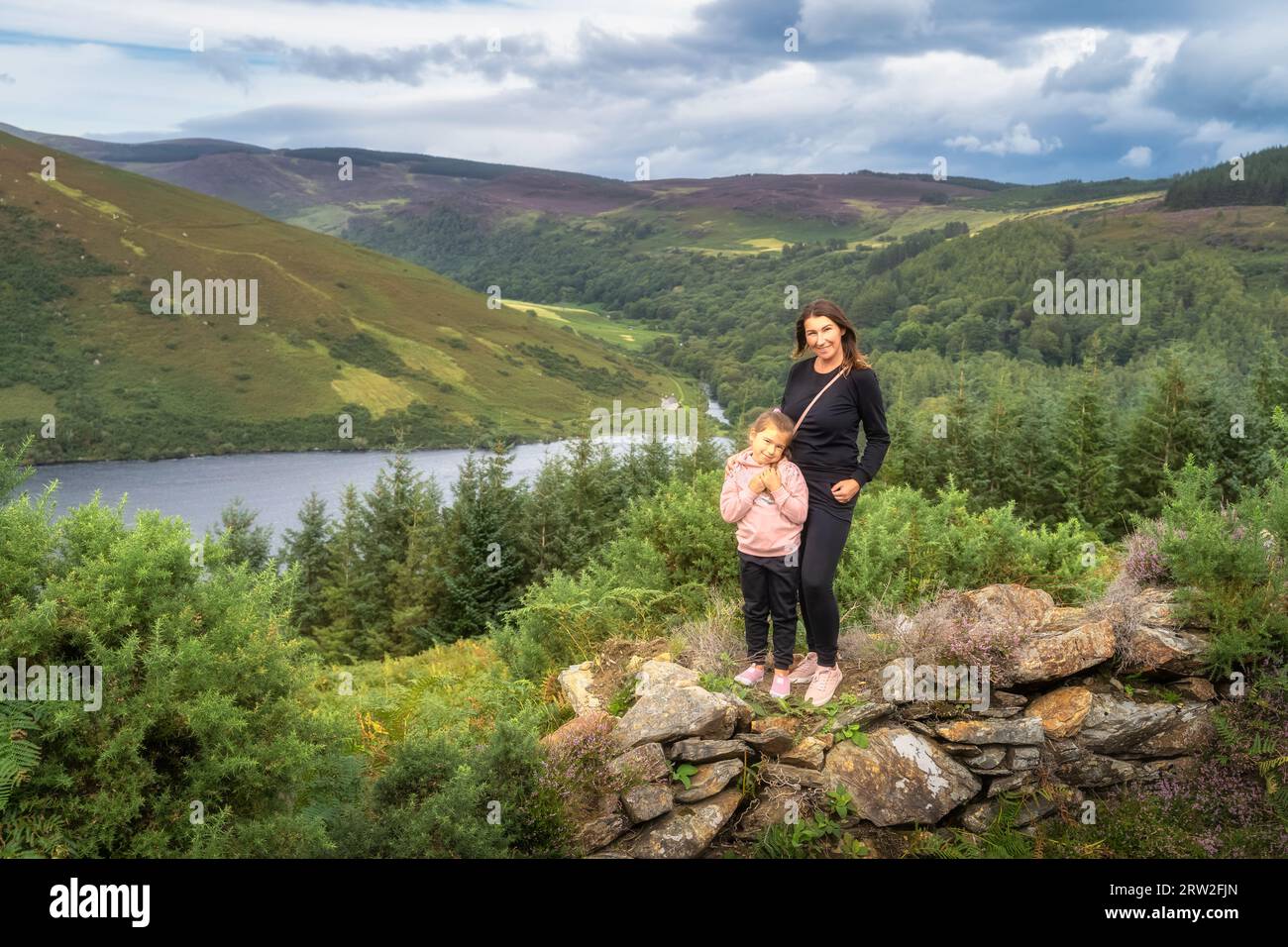 Mother and daughter standing and smiling on rock wall. Lake Lough Dan ...