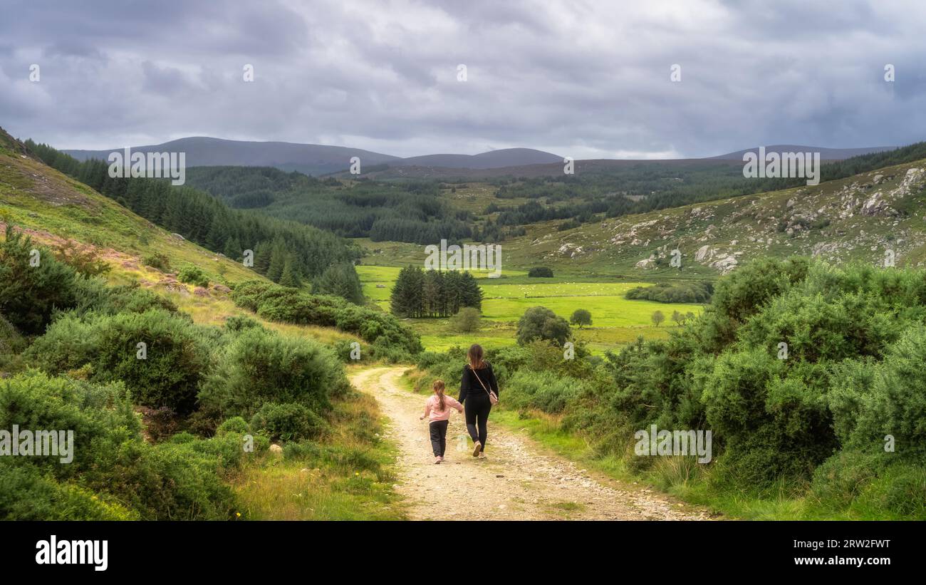 Mother and daughter walking down on country road towards green mountain ...