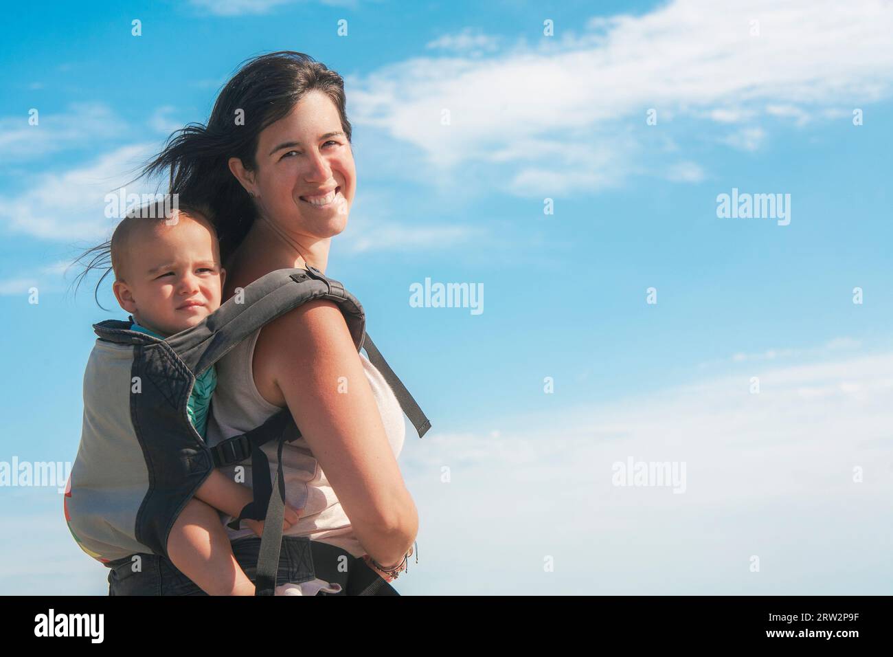 Mother with her child carried in a backpack on her back and a big smile ...