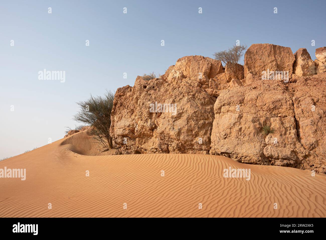 Rock formation surrounded by desert sand, under a vivid blue sky ...
