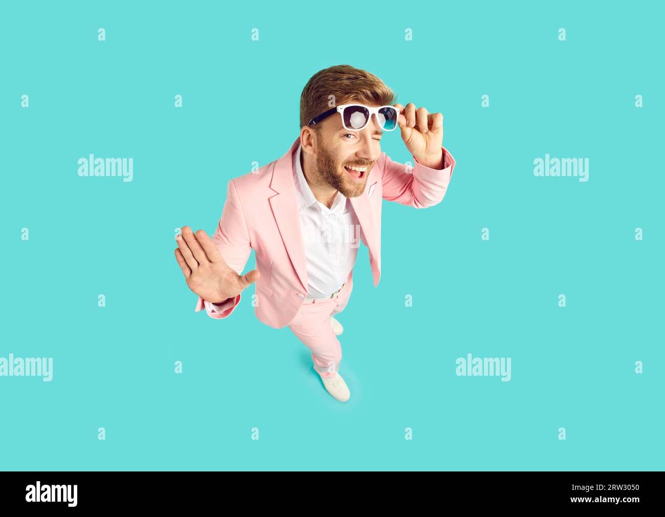 High angle of happy cheeky man in pink suit smiling, taking off ...