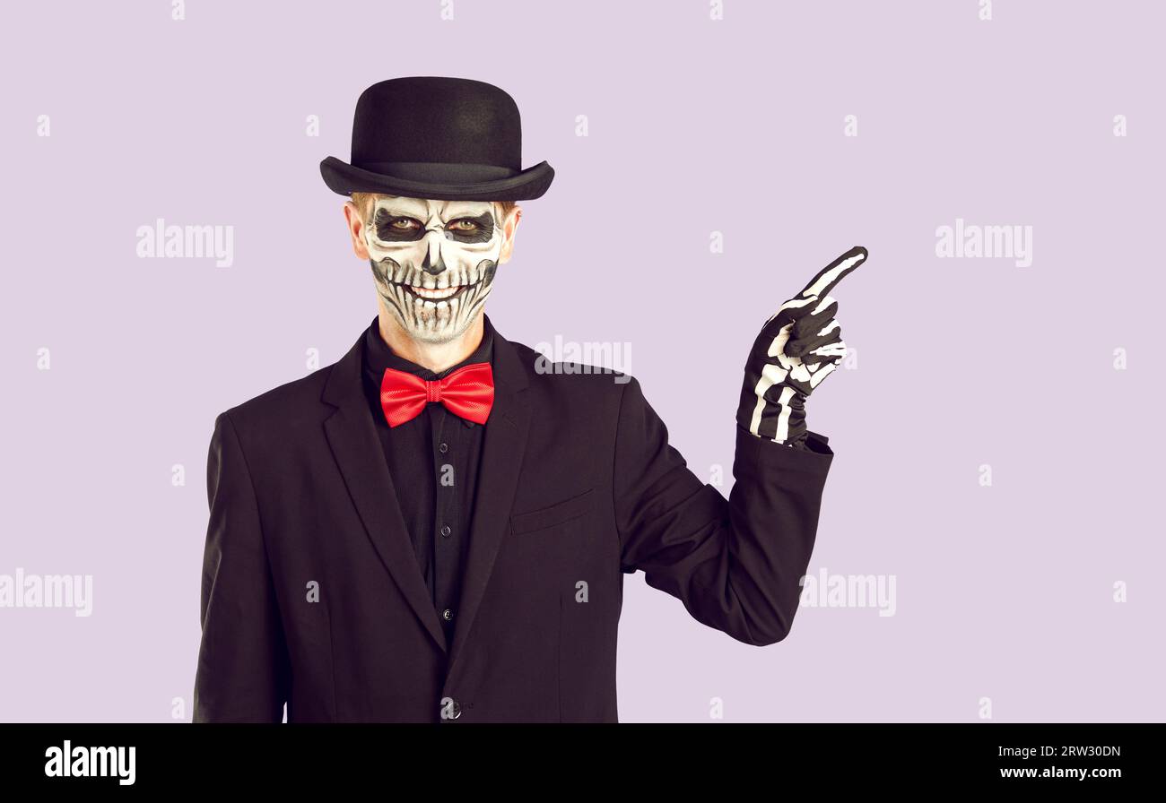 Portrait of spooky man with skull makeup pointing his finger to side ...