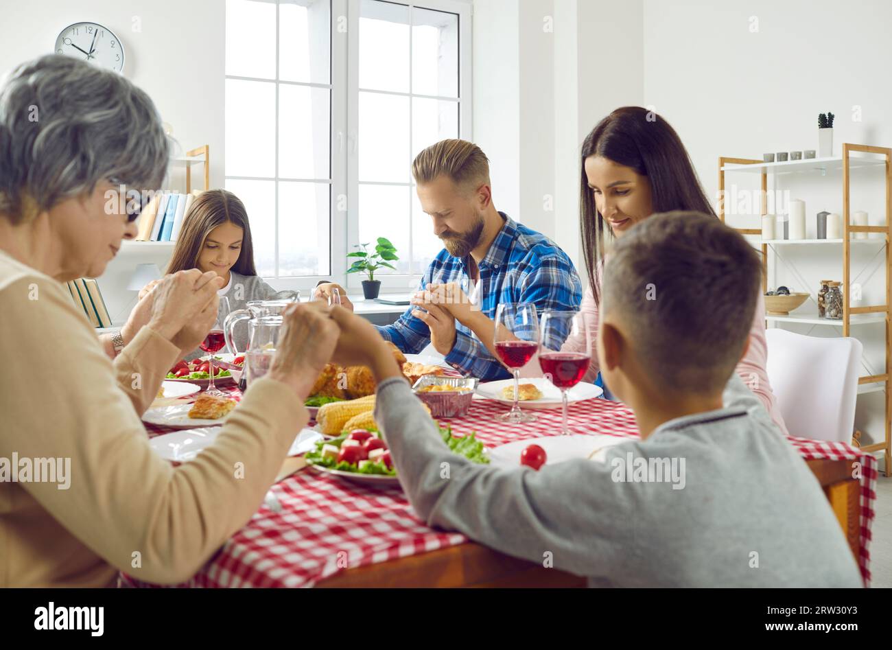 Family sitting around Thanksgiving table, holding hands, praying and ...