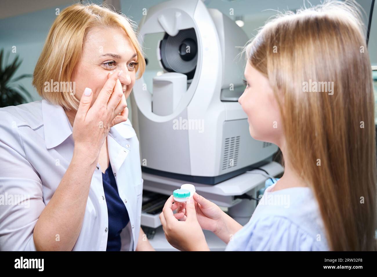 Experienced optician demonstrating little girl how to insert ophthalmic ...