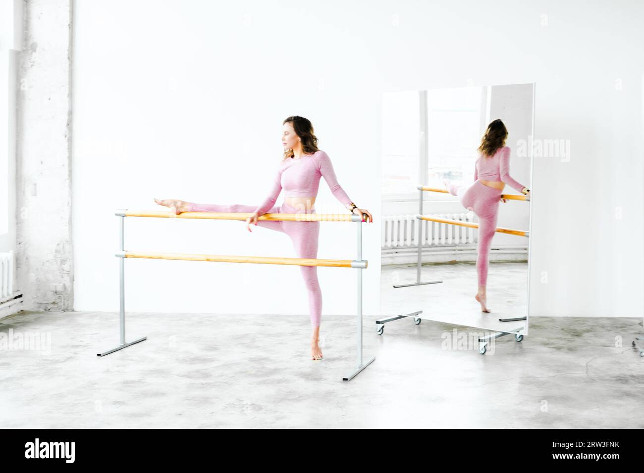 Slim ballerina woman girl in pink tracksuit. Stretching at ballet ...