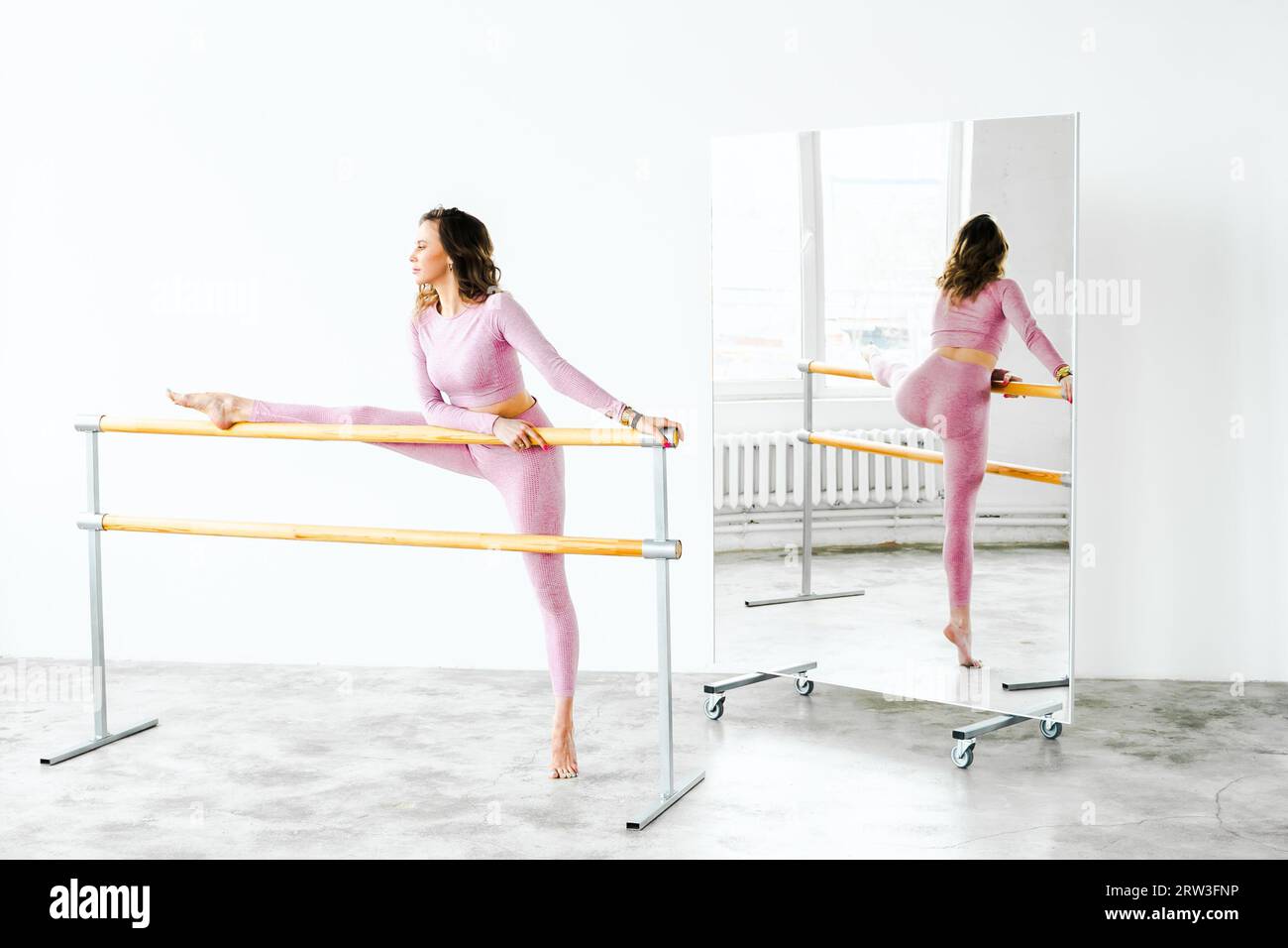 Slim ballerina woman girl in pink tracksuit. Stretching at ballet ...