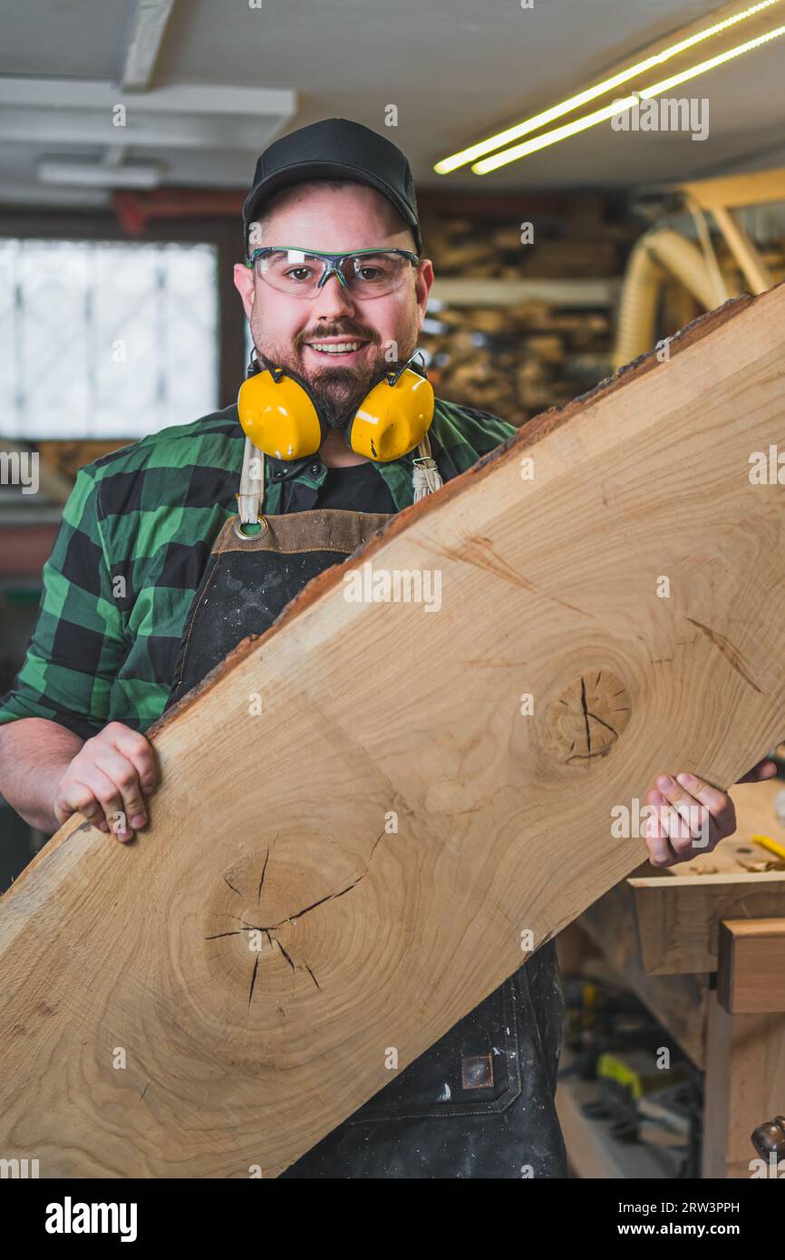 Portrait of male carpenter holding big wooden plank, workshop ...