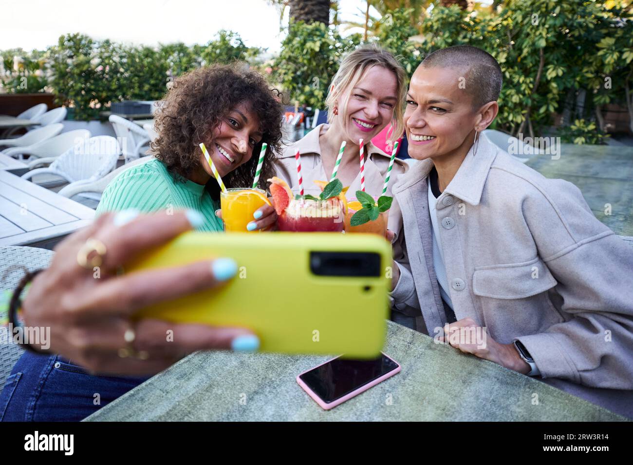 Mobile selfie three middle aged multiracial women looking smiling camera outdoor. Group cheerful ...