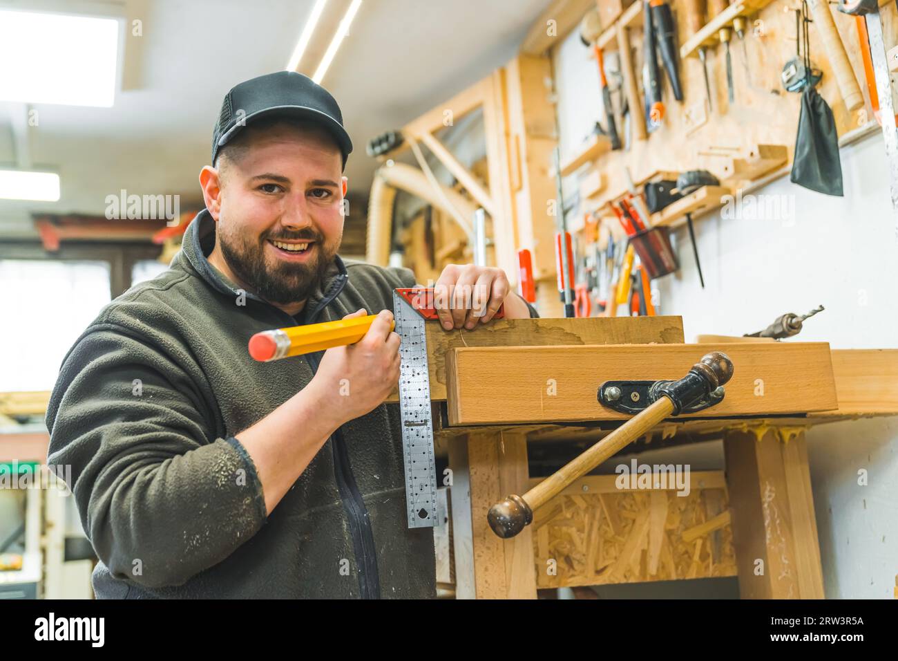A smiling craftsman marking measurement on wood with setsquare and a ...