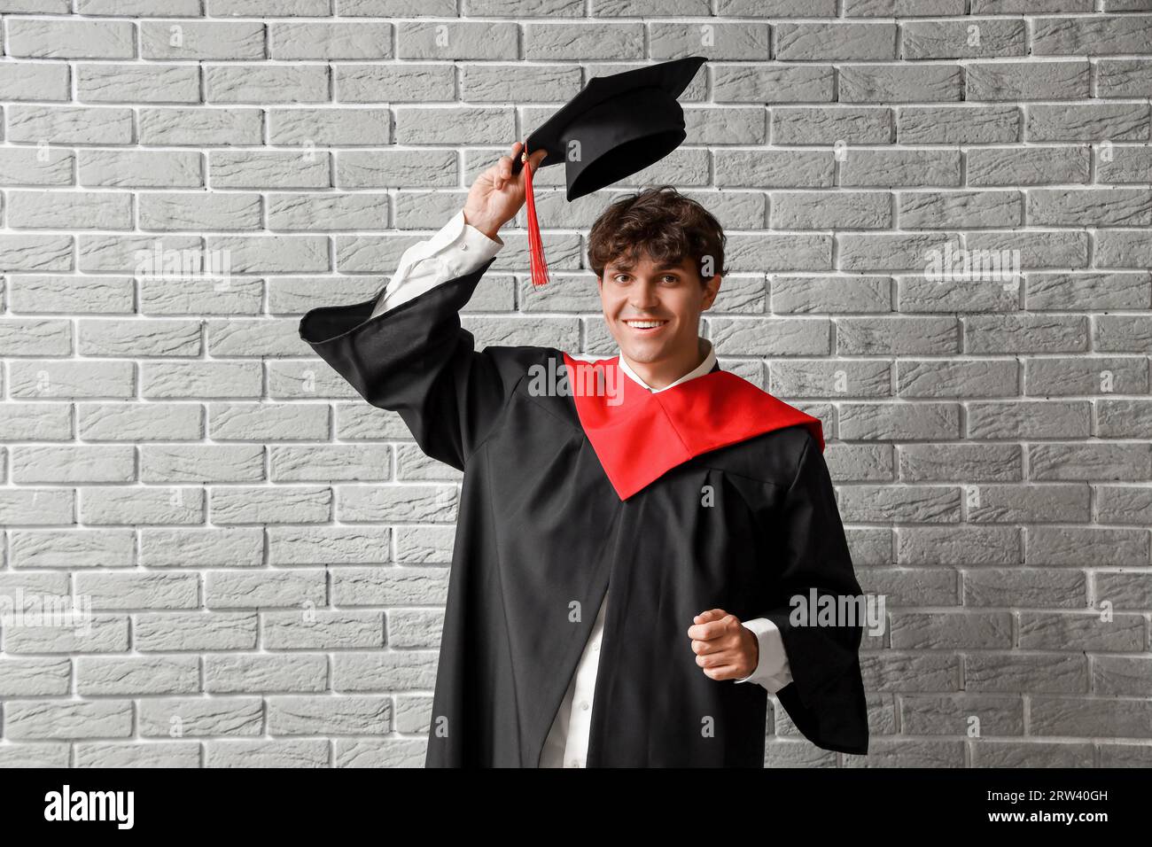 Male graduate student on grey brick background Stock Photo - Alamy