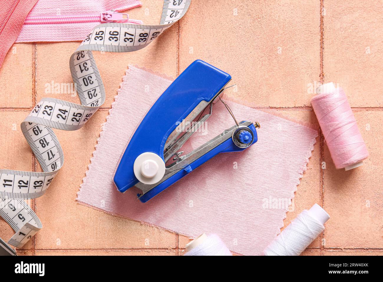 Manual sewing machine with different supplies on pink tile background ...