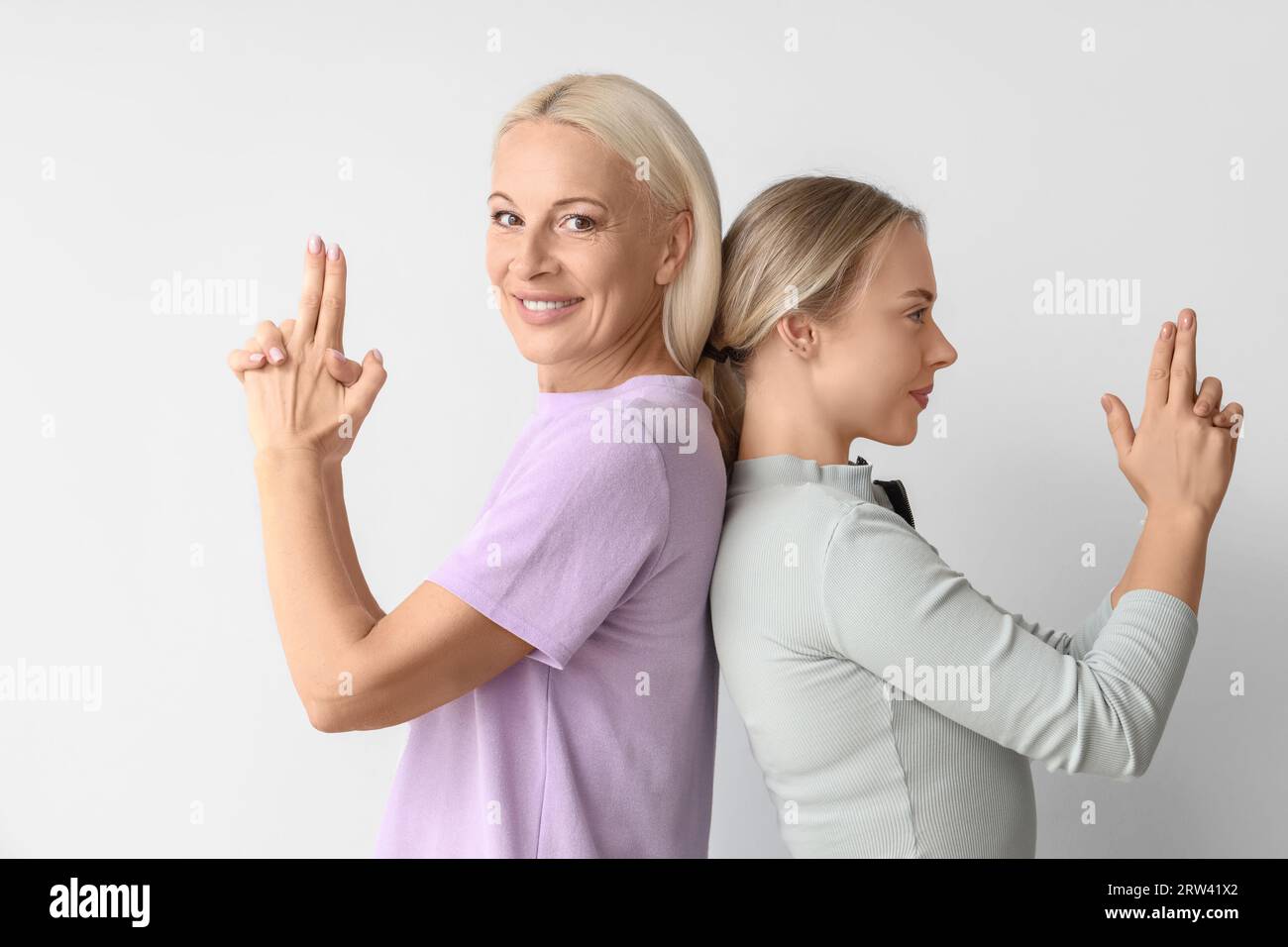 Happy young beautiful woman and her mother showing guns gesture on grey ...
