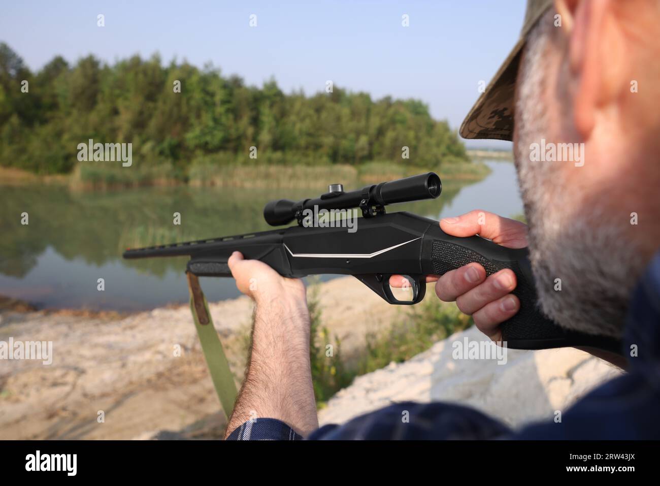 Man aiming with hunting rifle near lake outdoors, closeup Stock Photo ...